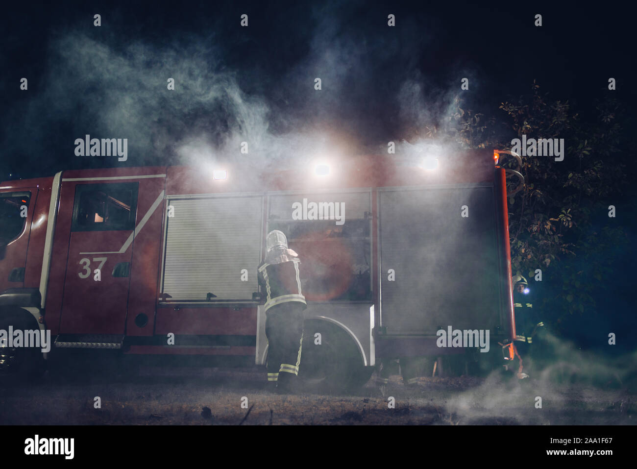 Group of firemen putting out a fire with a long water hose Stock Photo ...