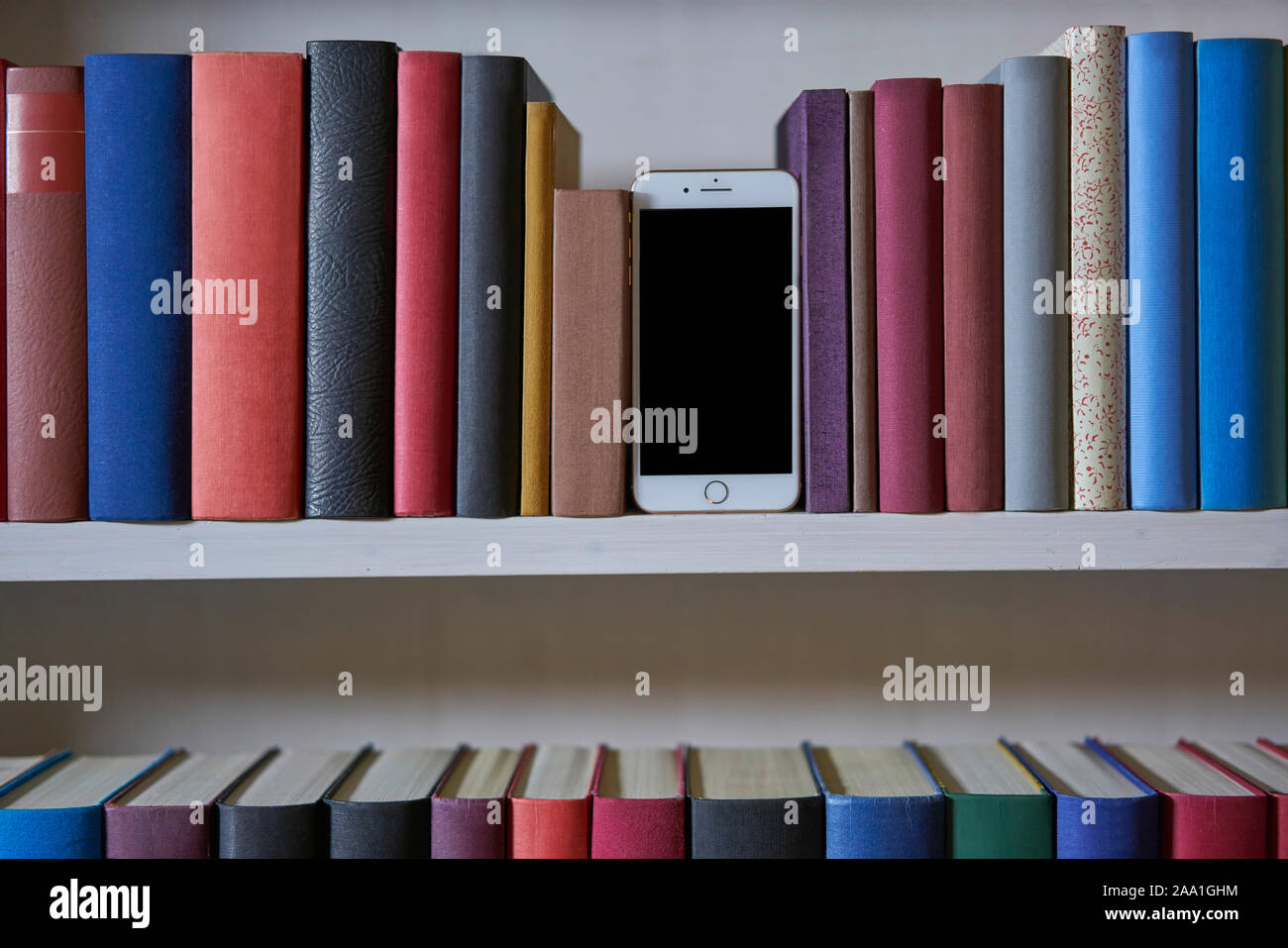 Mobile phone between colourful books in a shelf, front view Stock Photo ...