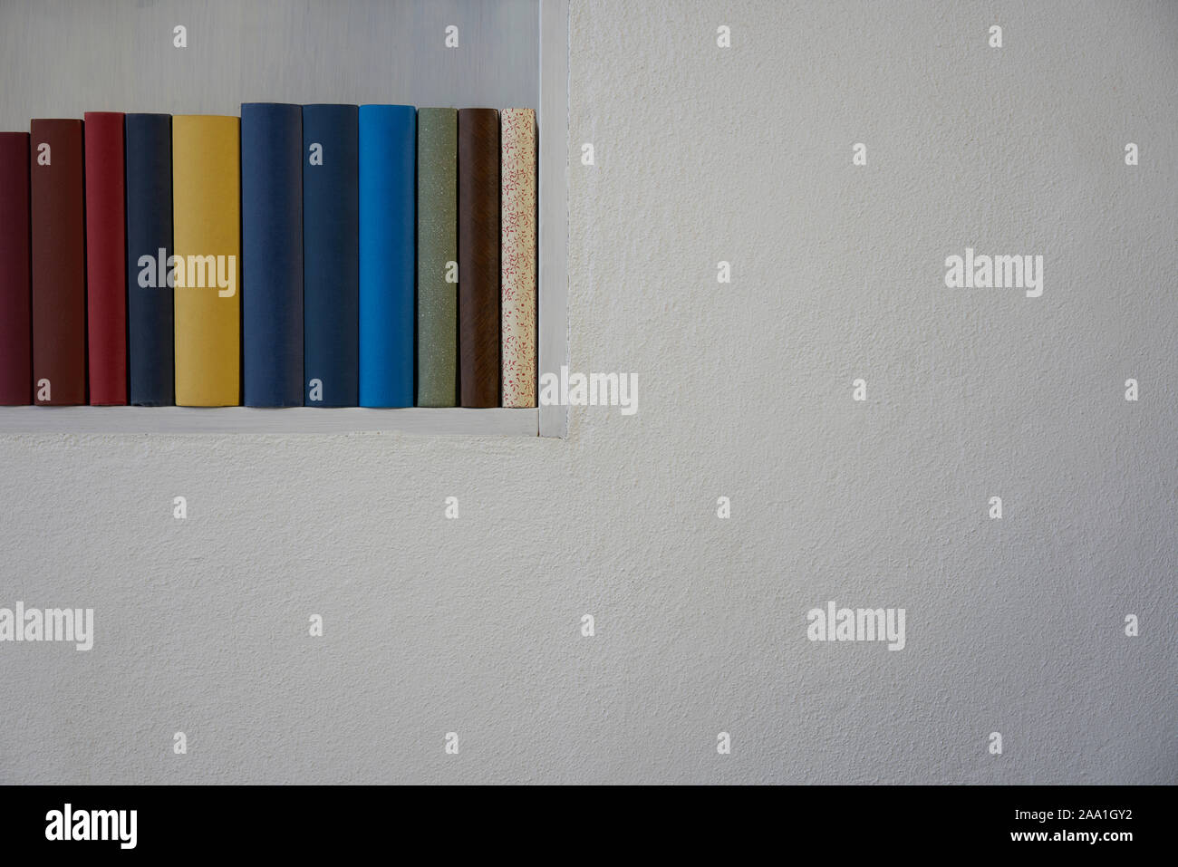 Detail of a row of colorful book covers in a shelf in a white wall ...