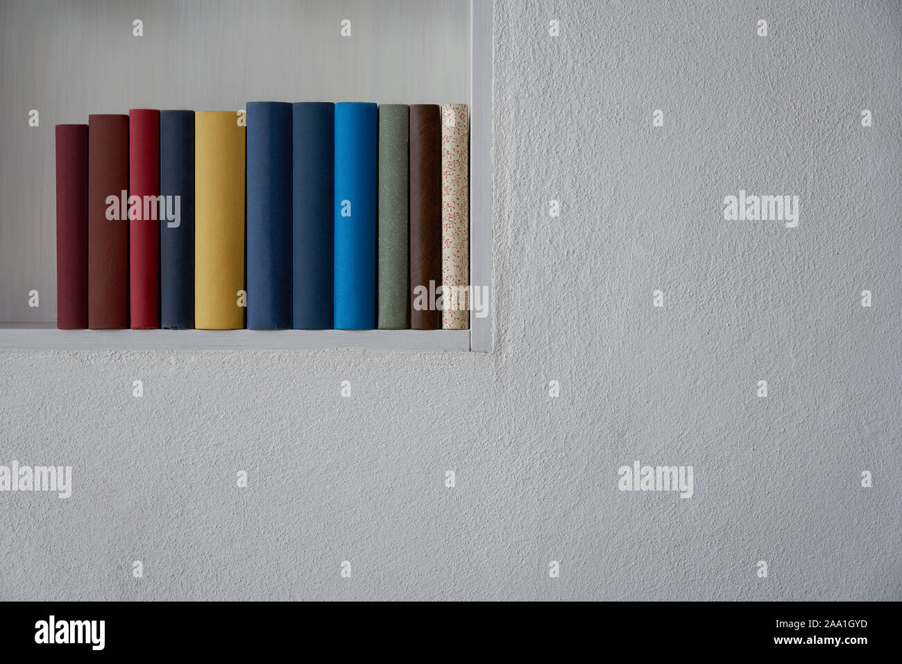 Detail of a row of colorful book covers in a shelf in a white wall ...