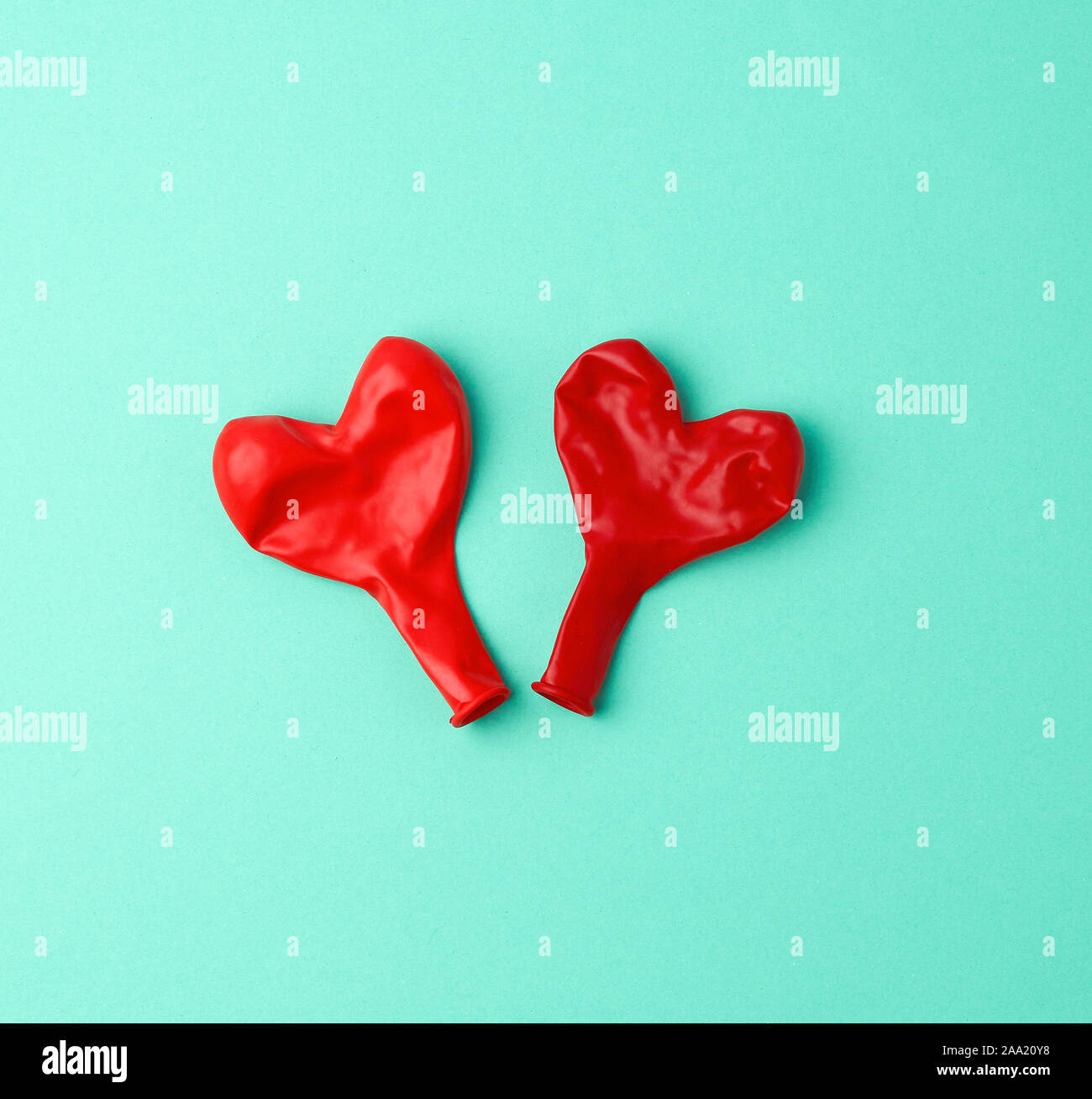 two red rubber balloons blow away in the shape of a heart on a green ...