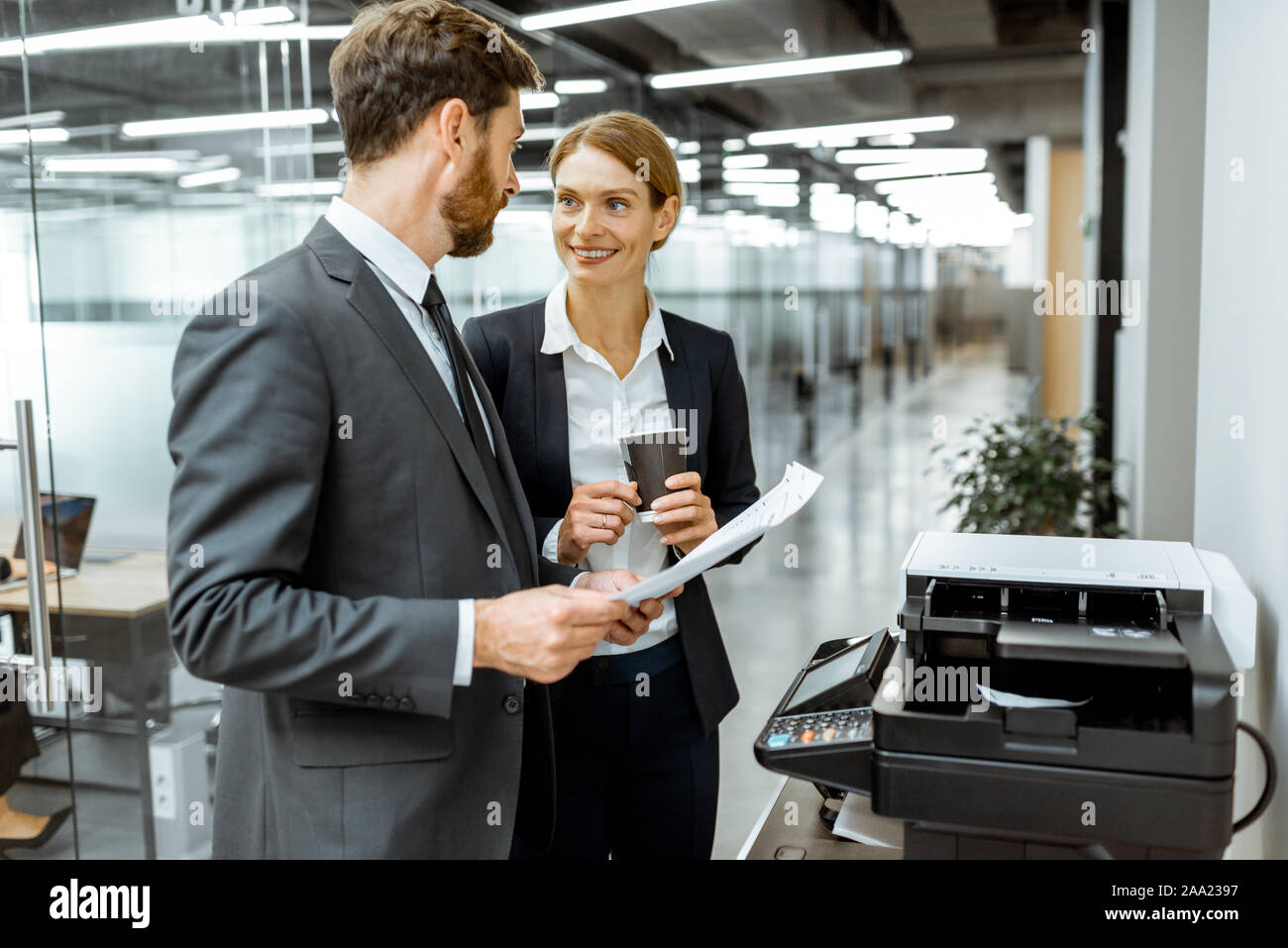Business man and woman talking near the copier during a coffee break in ...