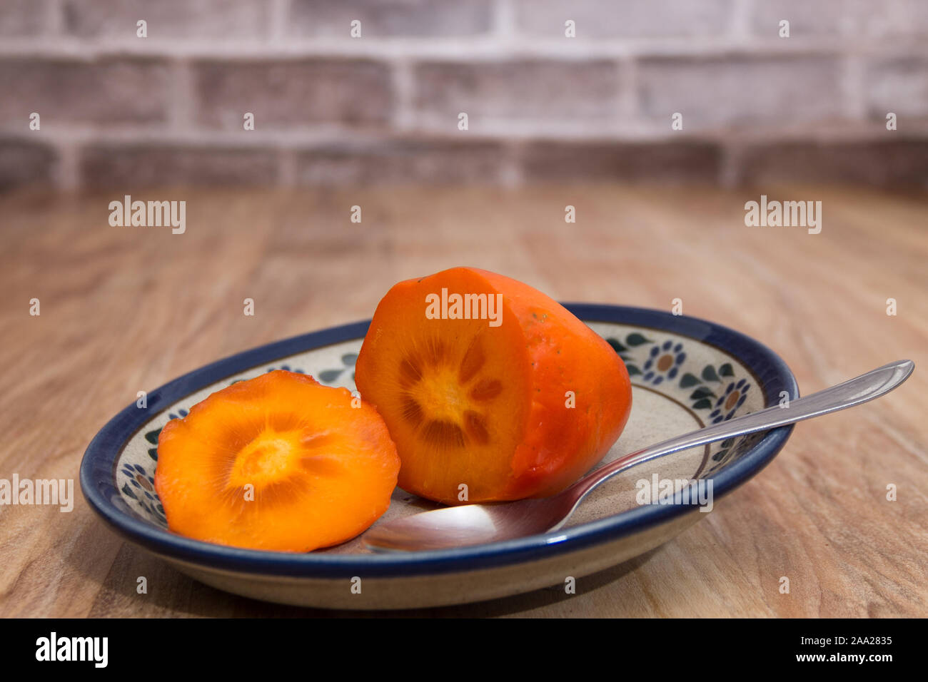 persimmon cut ready to eat, on rustic plate over wooden table with ...