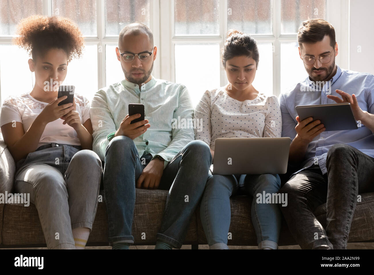 Concentrated diverse people sitting together on sofa, using different ...