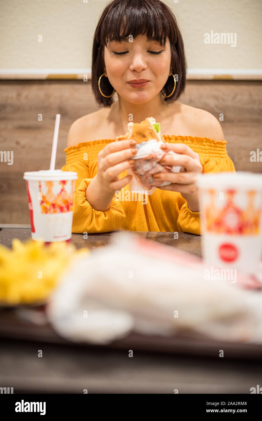 Beautiful young cute girl in fashionable clothes enjoys fast food ...