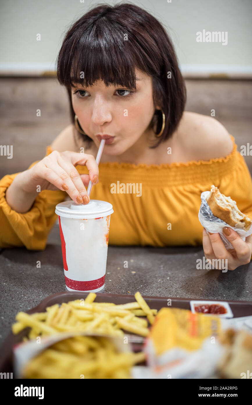 Beautiful young cute girl in fashionable clothes enjoys drink and fast ...