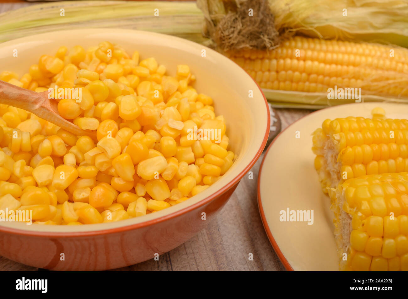 Grains of sweet corn in a plate and ears of corn on the wood table ...