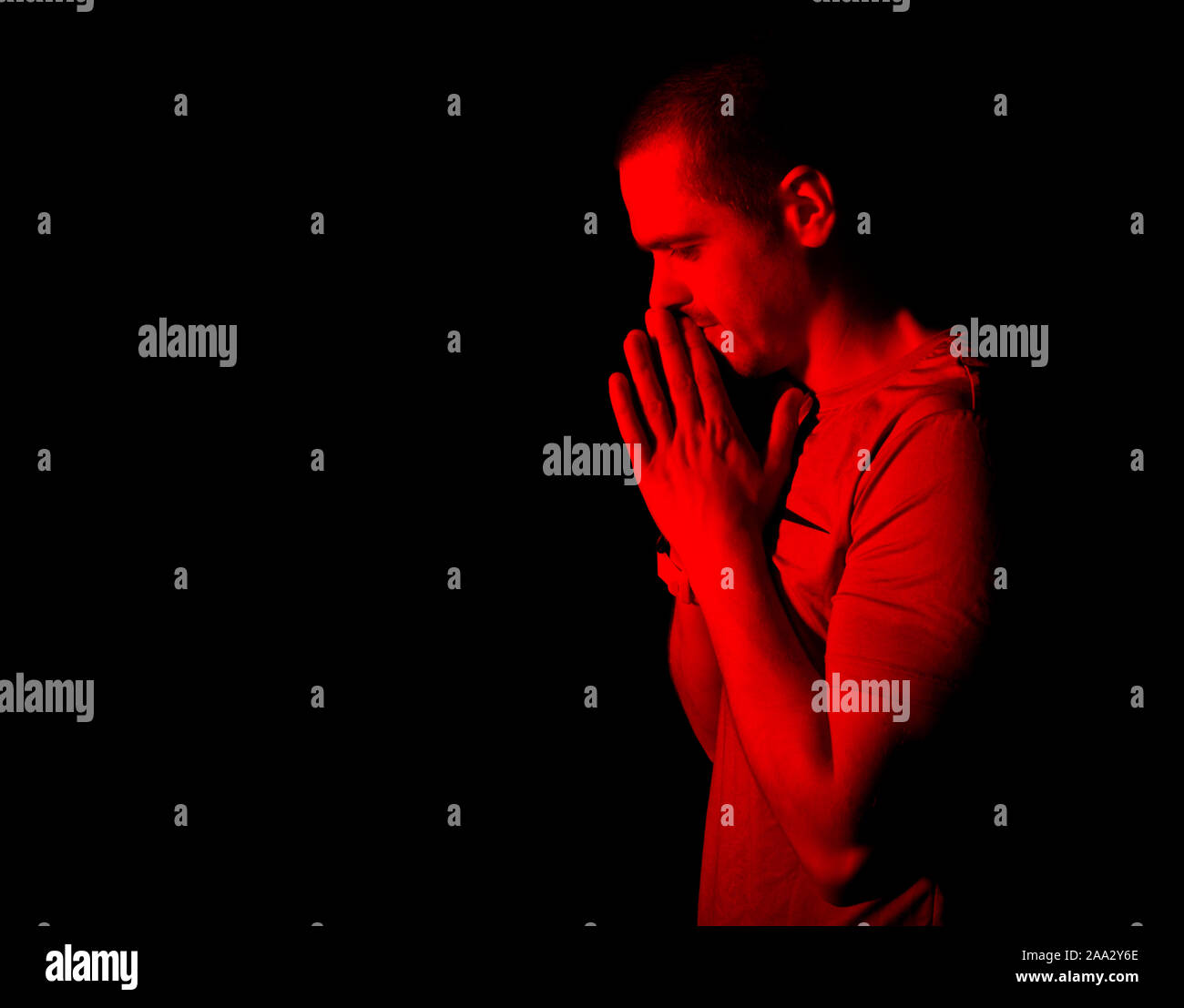 Praying man in red light standing in studio Stock Photo - Alamy