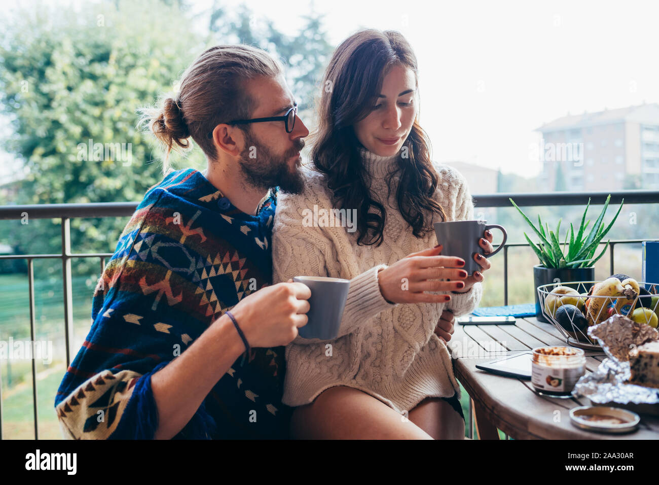 Young couple at home terrace having breakfast - she is sitting on his ...