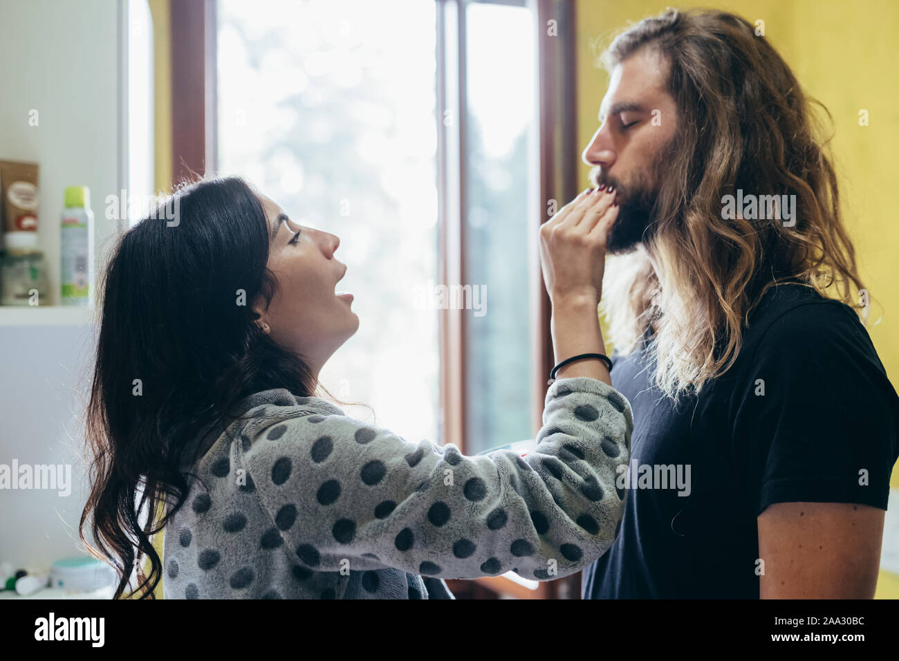 Beautiful woman putting on moisturizer on boyfriend in bathroom at home ...