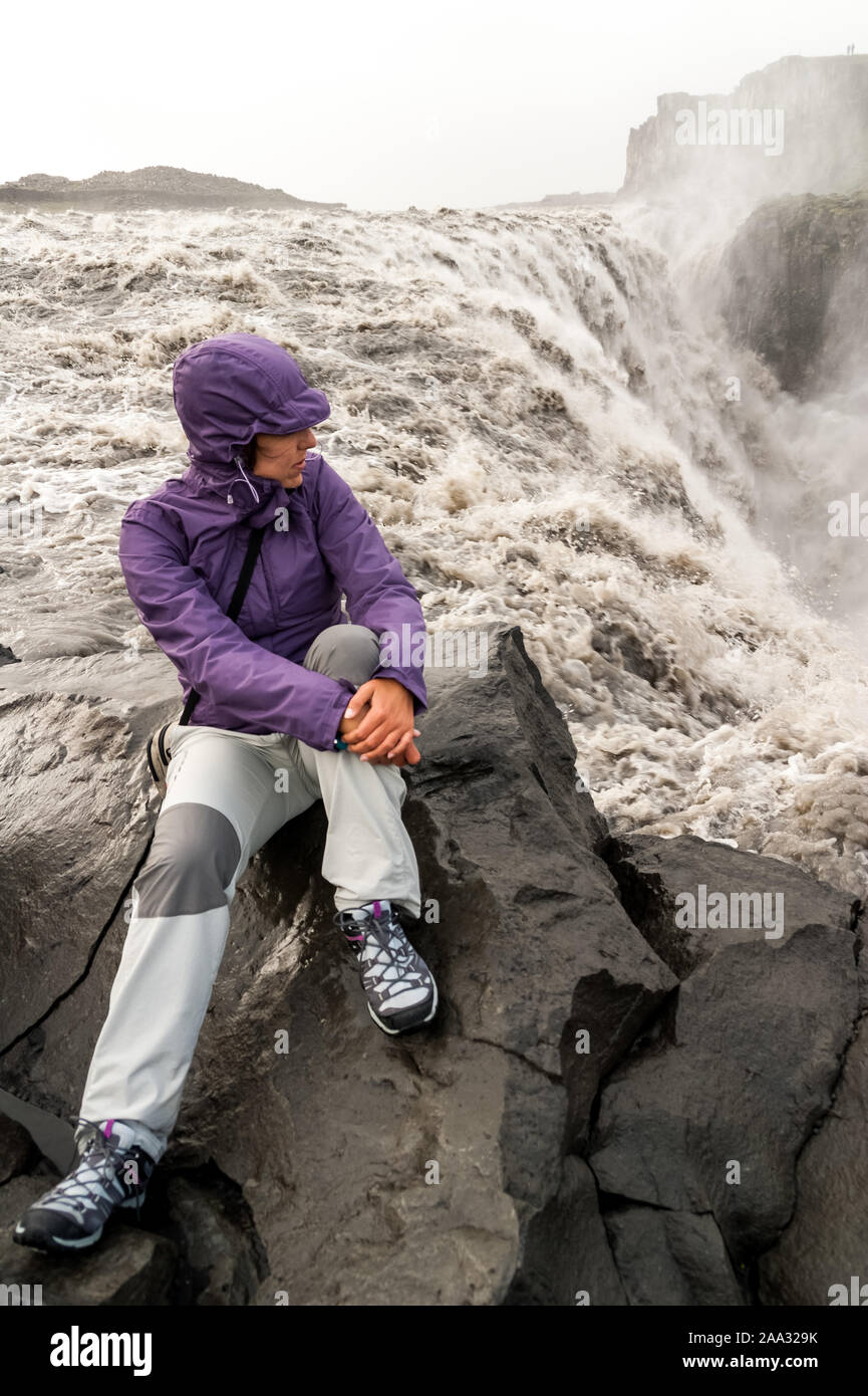 Adventurous woman is sitting next to the great Dettifoss waterfall in ...