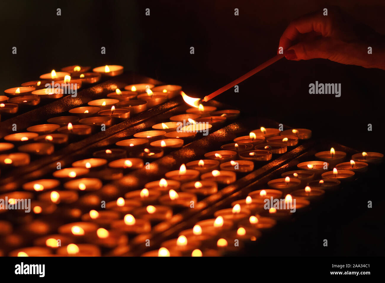 Hand lighting long candle in church. Rows of flames of candles in ...
