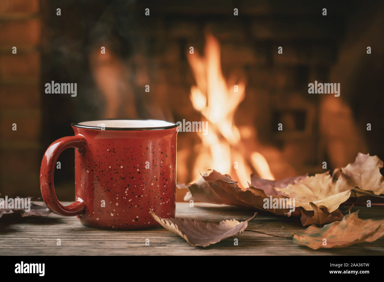 Red mug with hot tea in front of a burning fireplace, comfort and ...