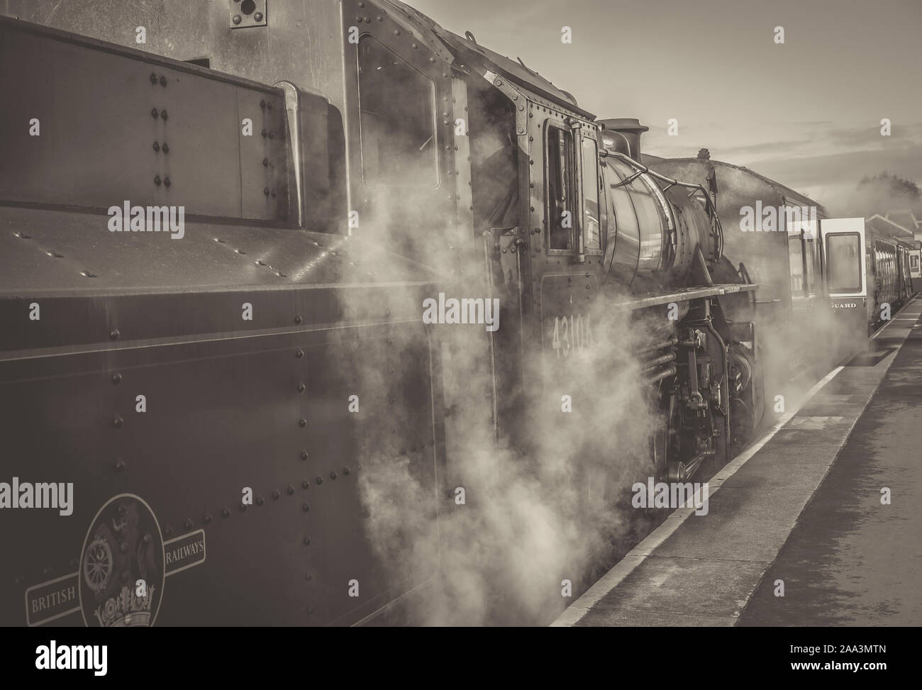 Vintage UK steam train waiting by platform letting off steam, crew in ...