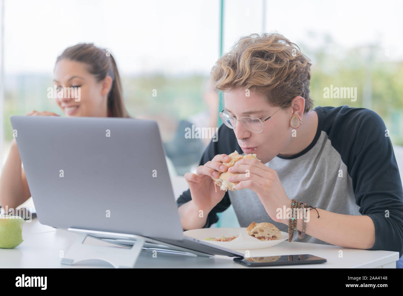Young man who is eating a sandwich in front of a computer. Concept work ...