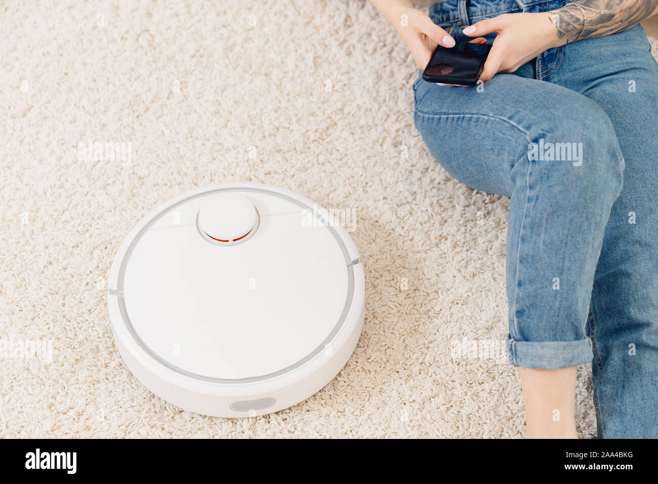Young girl using automatic smart robot vacuum cleaner working on carpet ...