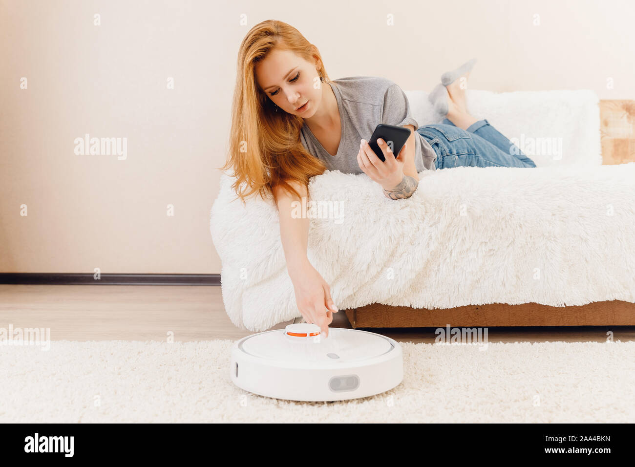Young girl using automatic smart robot vacuum cleaner working on carpet ...