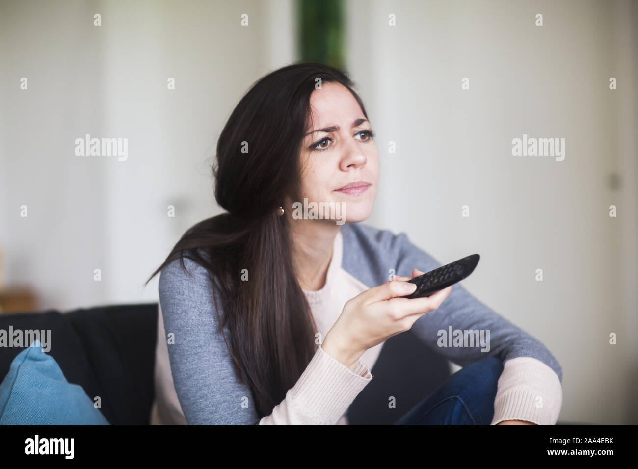 Woman sitting on sofa using a remote control Stock Photo - Alamy