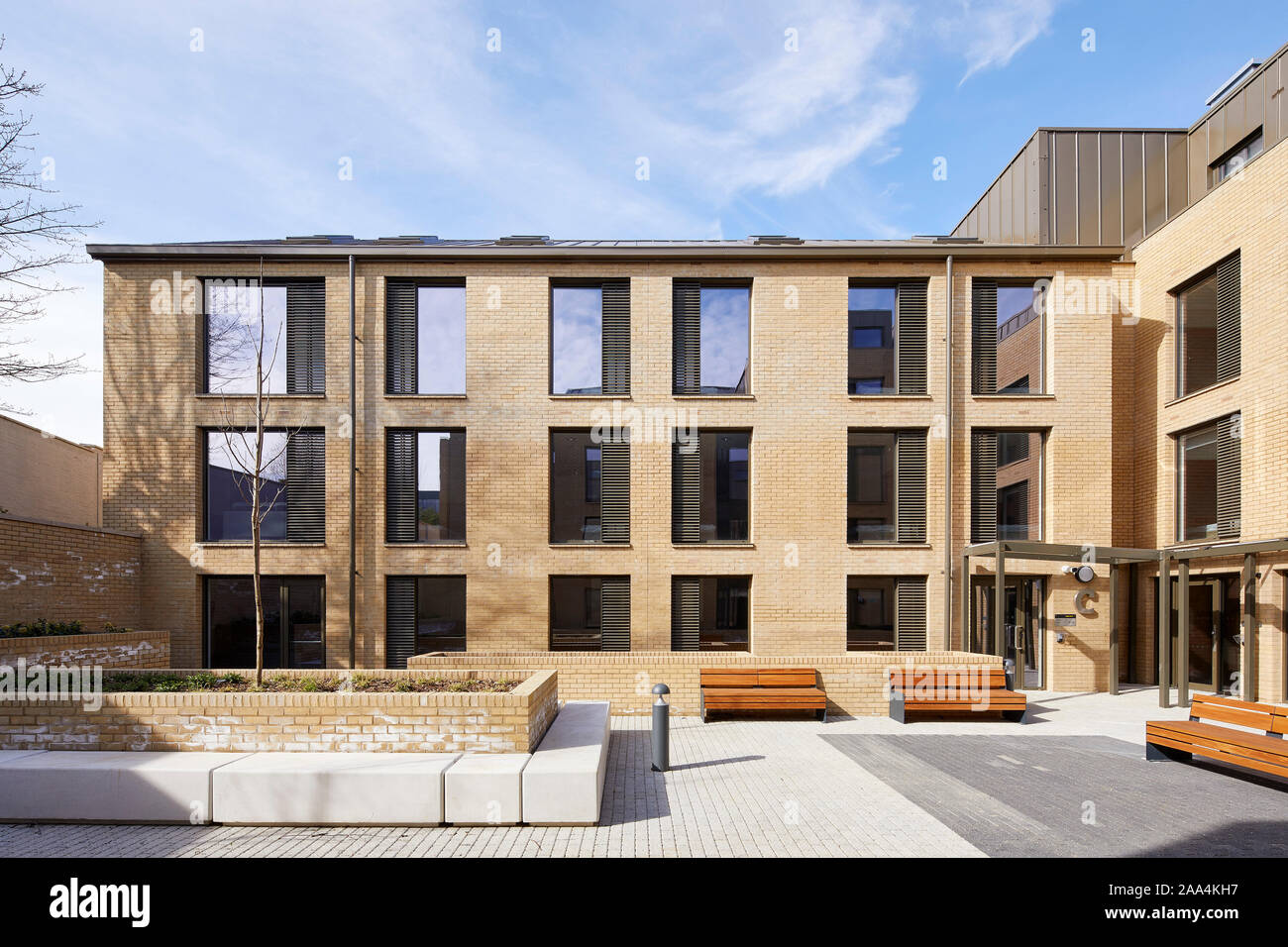 Front view towards brick facade with planters and timber benches ...