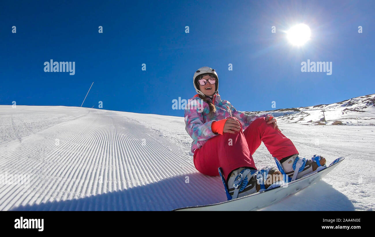 Snowboarding girl in pink trousers and helmet sitting on a perfectly ...