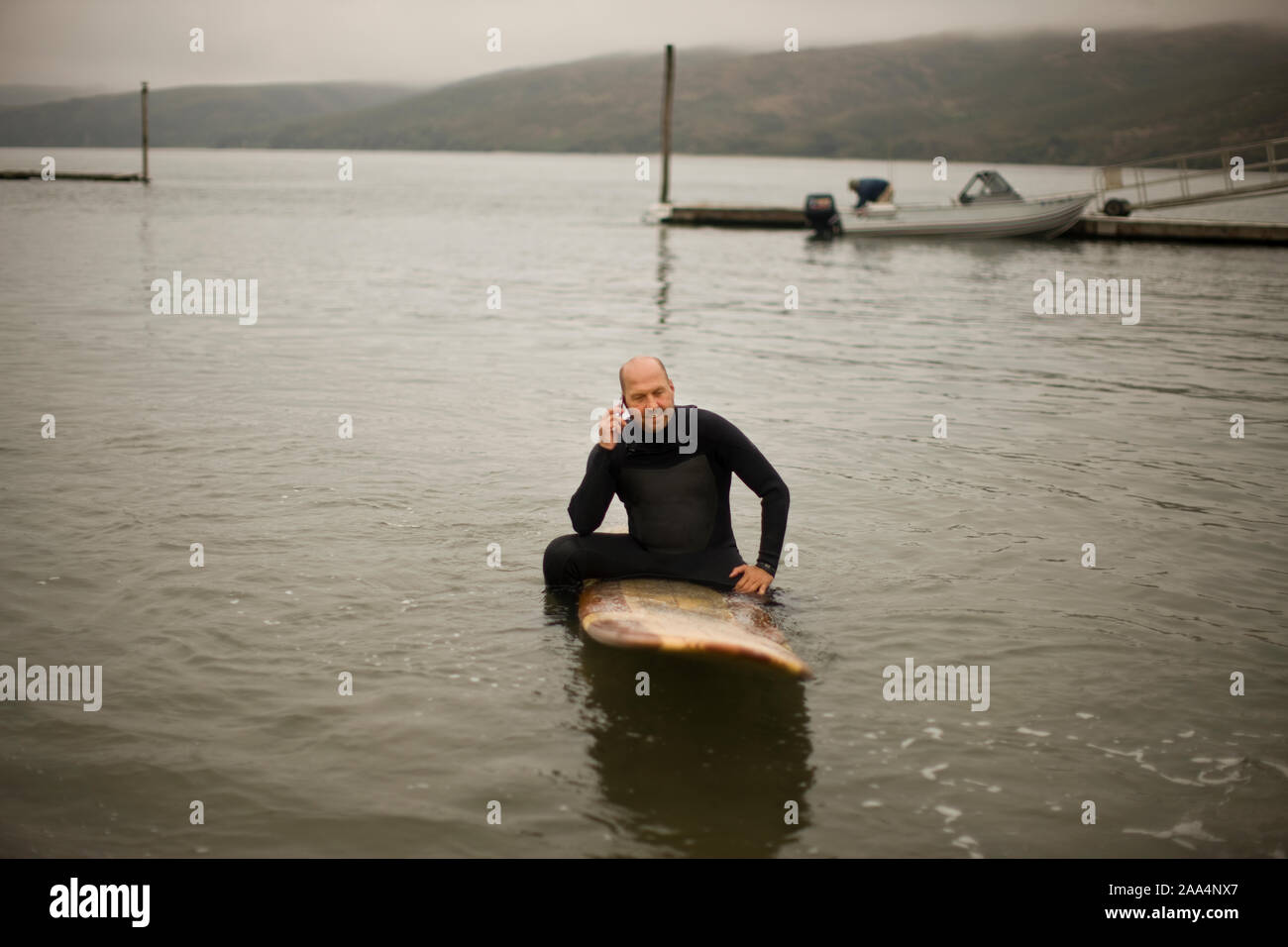 Man talking on mobile phone while sitting on surfboard Stock Photo - Alamy