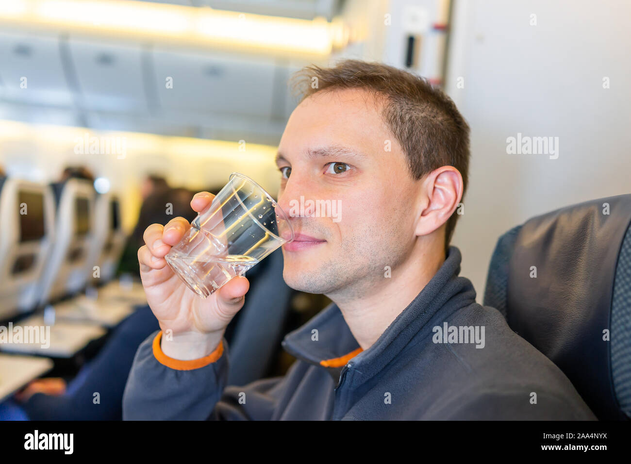 Happy young man drinking water in plastic cup flying in economy seat ...