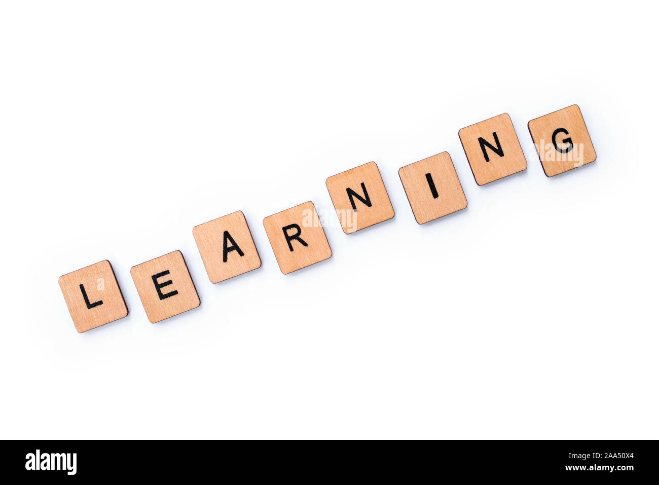 The word LEARNING, spelt with wooden letter tiles over a white ...