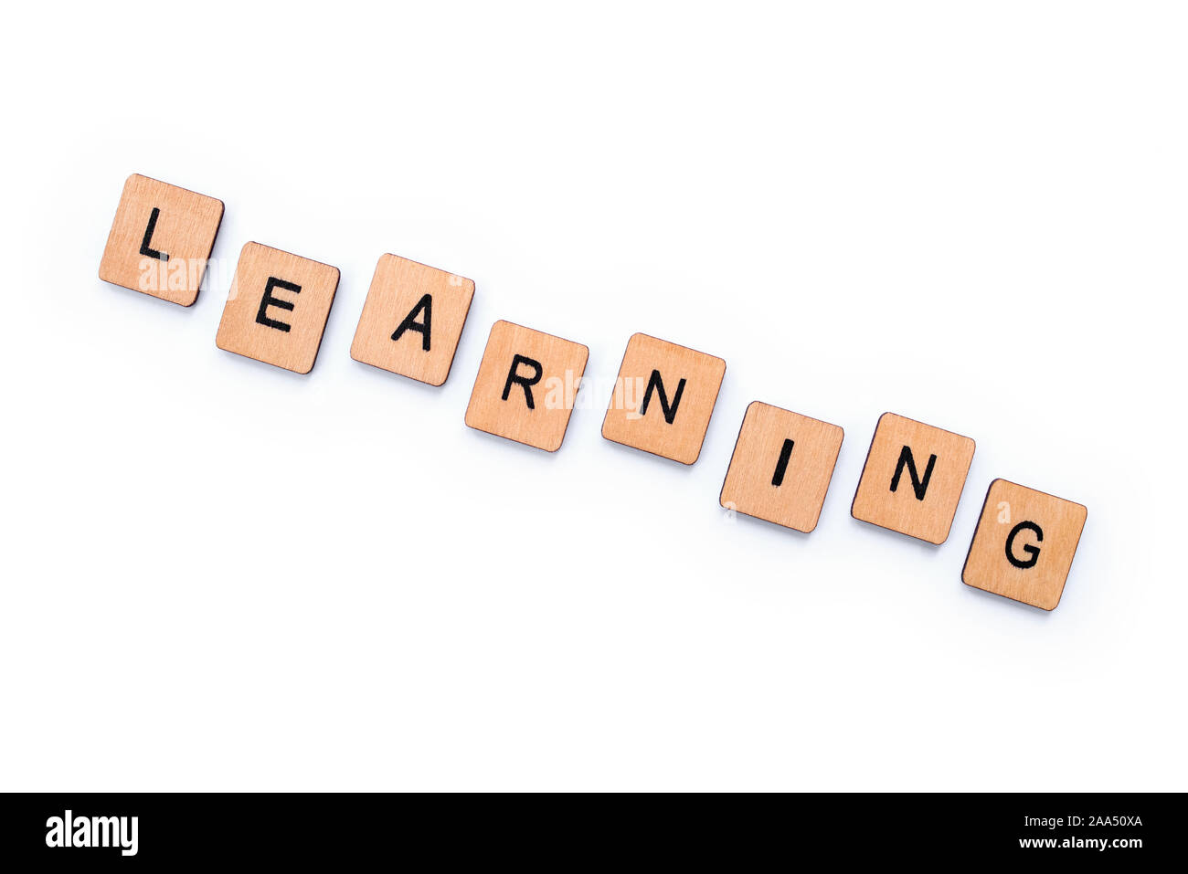 The word LEARNING, spelt with wooden letter tiles over a white ...