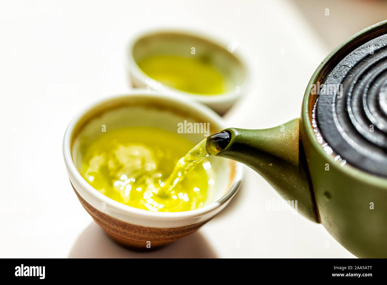 Green tea clay teapot on white table background and pouring liquid ...