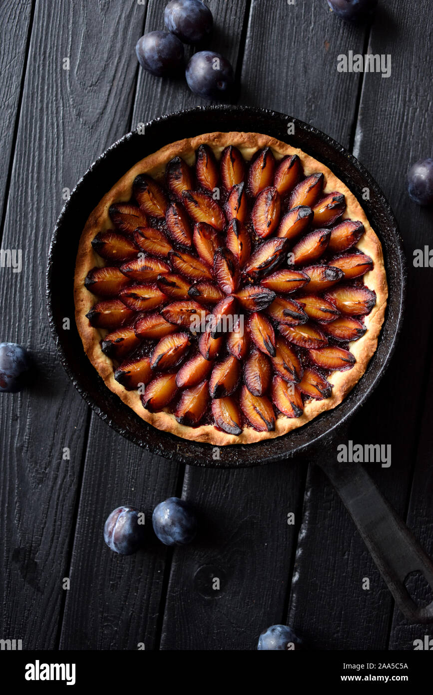 Cooking failure. Burned plum pie in cast iron pan on black background ...