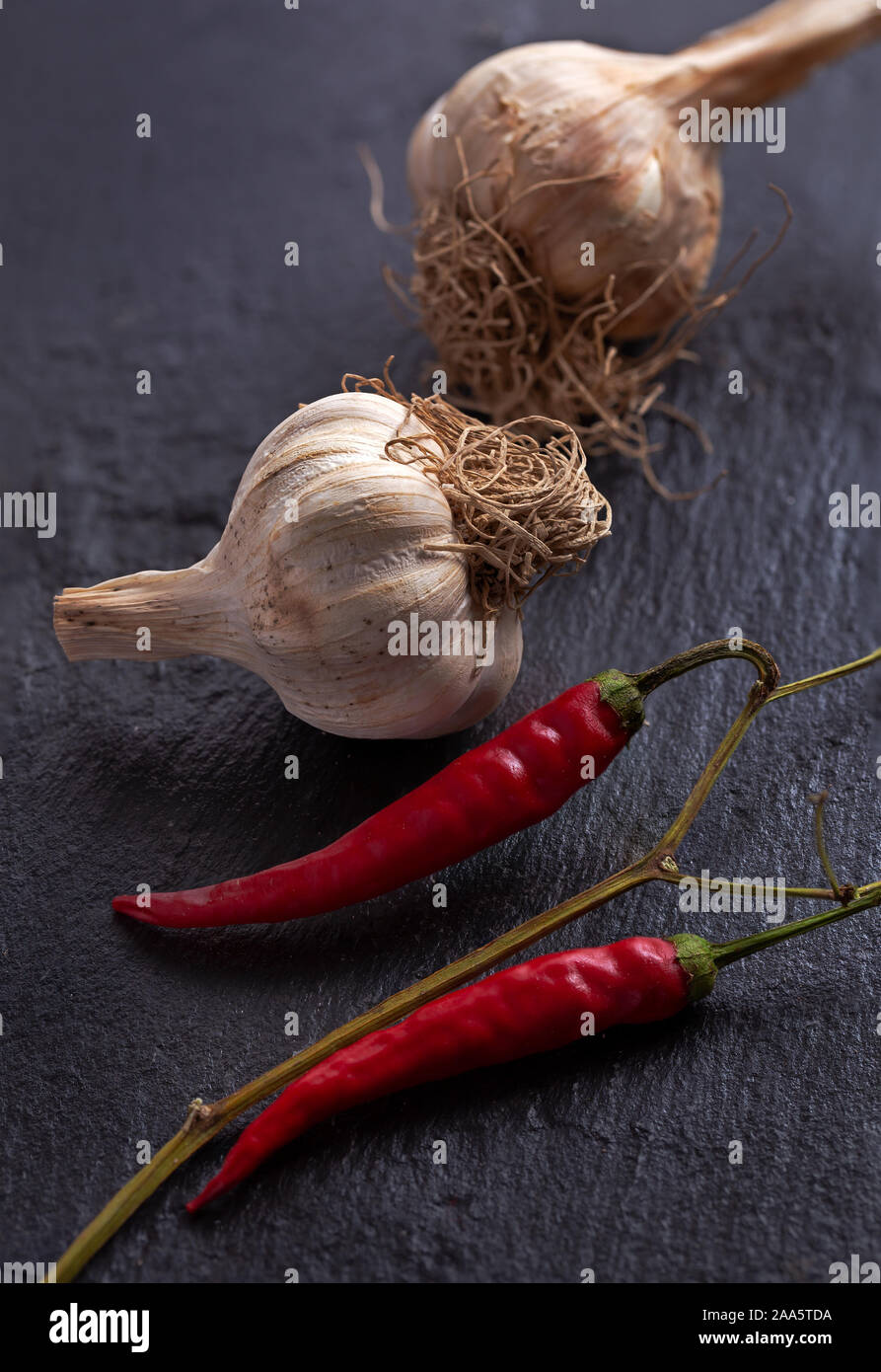 Two garlic bulbs and red chili peppers on a dark surface Stock Photo ...