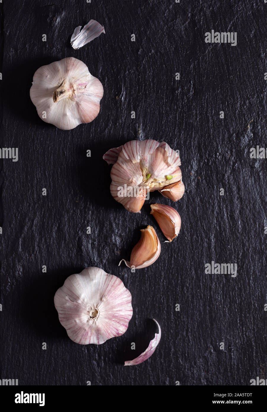 Overhead view of three bulbs of raw purple garlic on a black surface ...