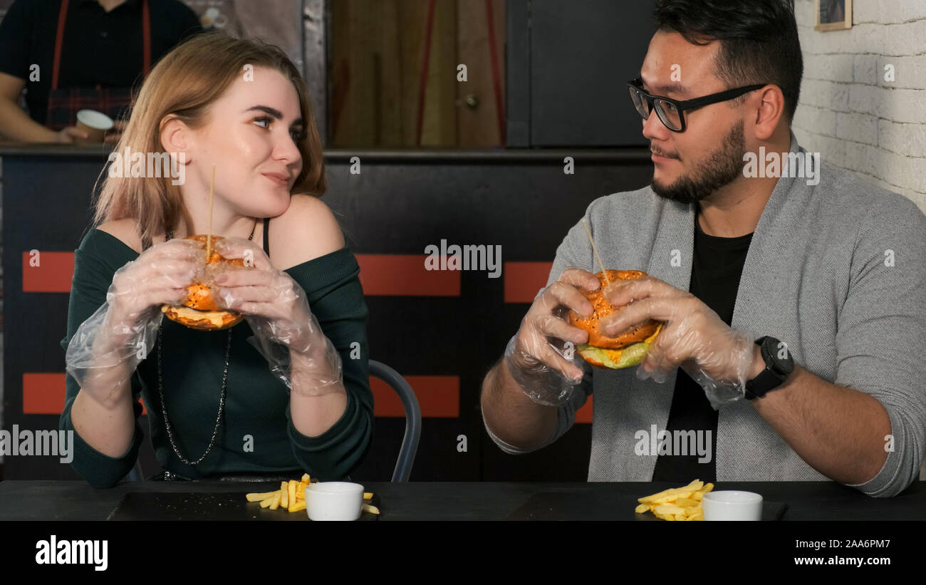 Multiracial couple eating burgers in a cafe Stock Photo - Alamy