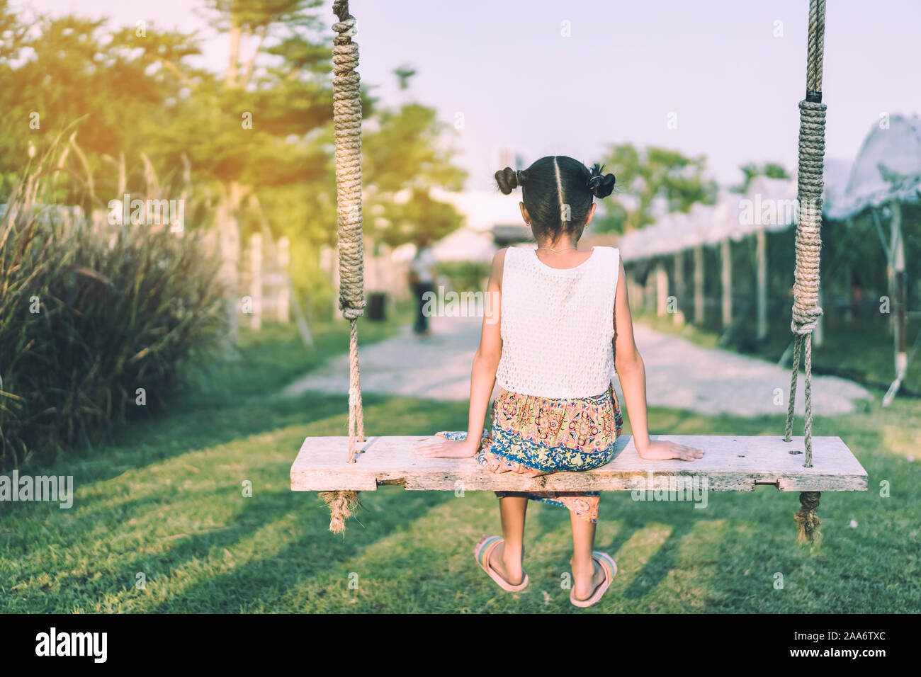 Back view of young girl sit on swings for wait her mom in the organic ...