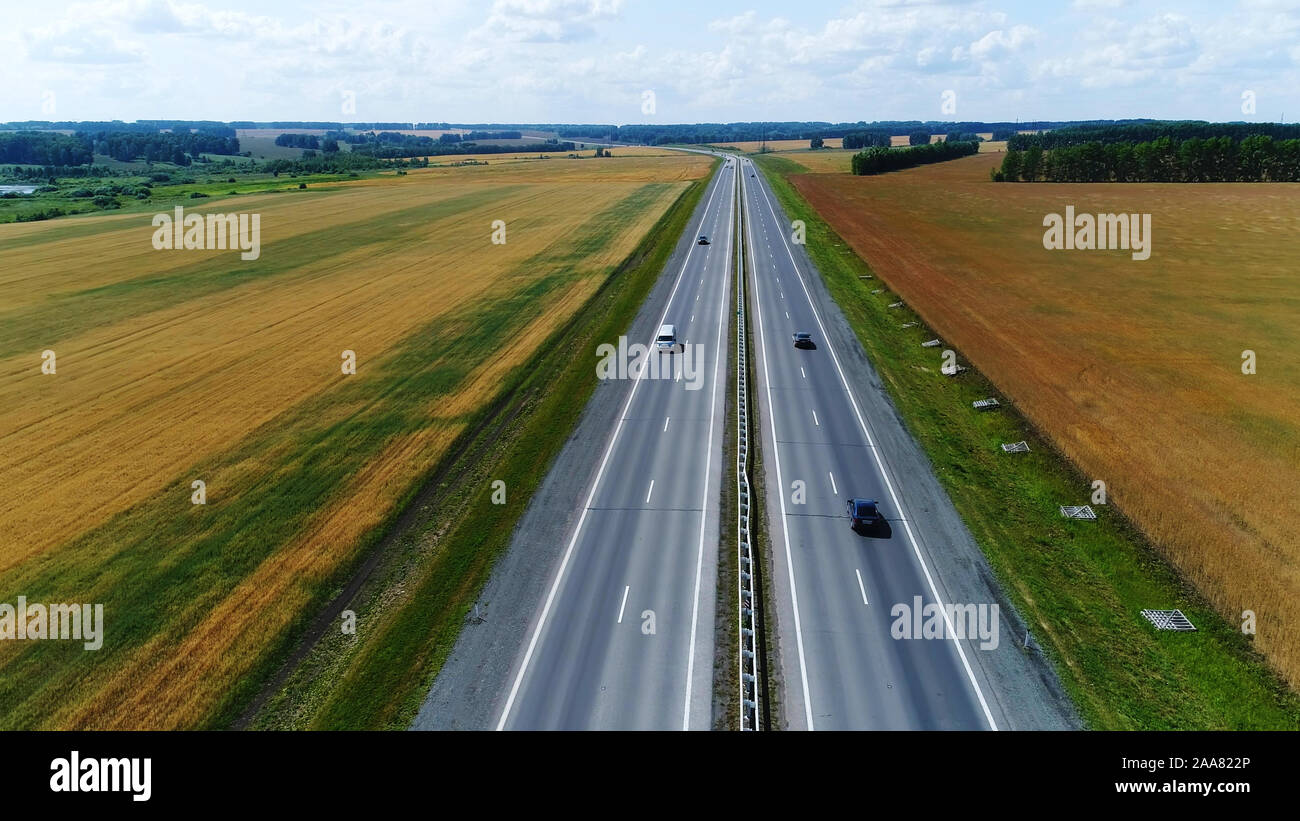 Aerial view Drone flies back over the highway through the fields. Cars ...