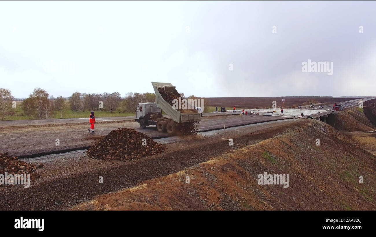 Aerial view construction of a new highway. Trucks pour crushed stone on ...