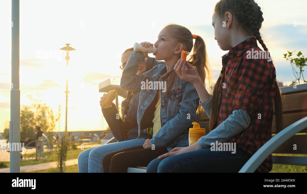 Three schoolgirls friends are sitting on a bench and eating. School ...