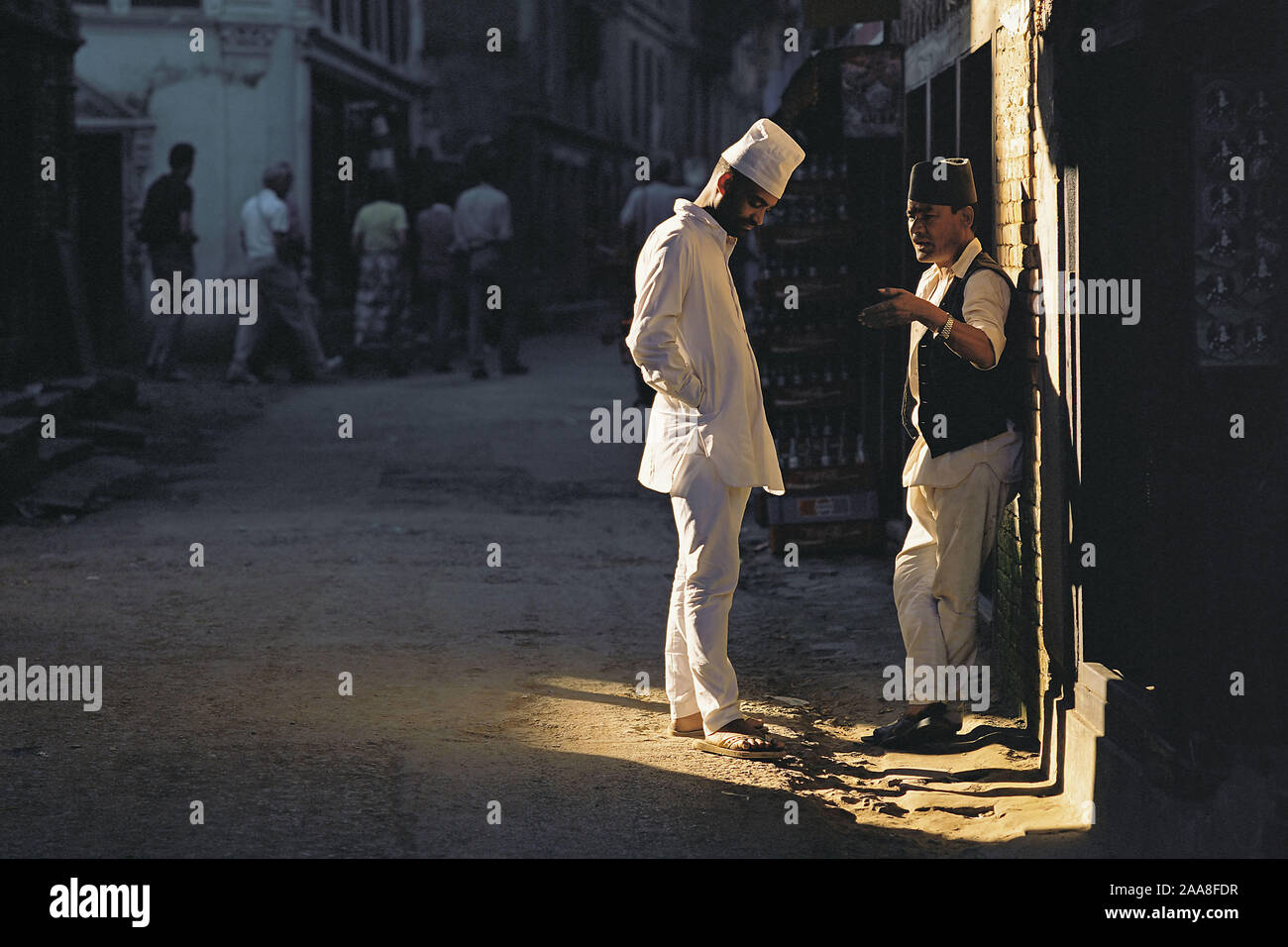 Two men chat in a patch of sunlight in a Kathmandu backstreet ...