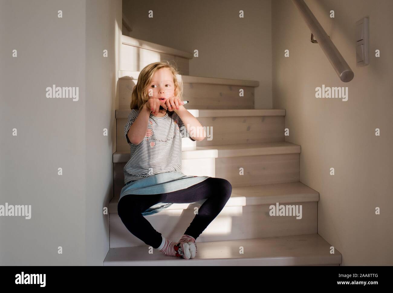 young girl pulling a cat face after drawing a cat on her face at home ...