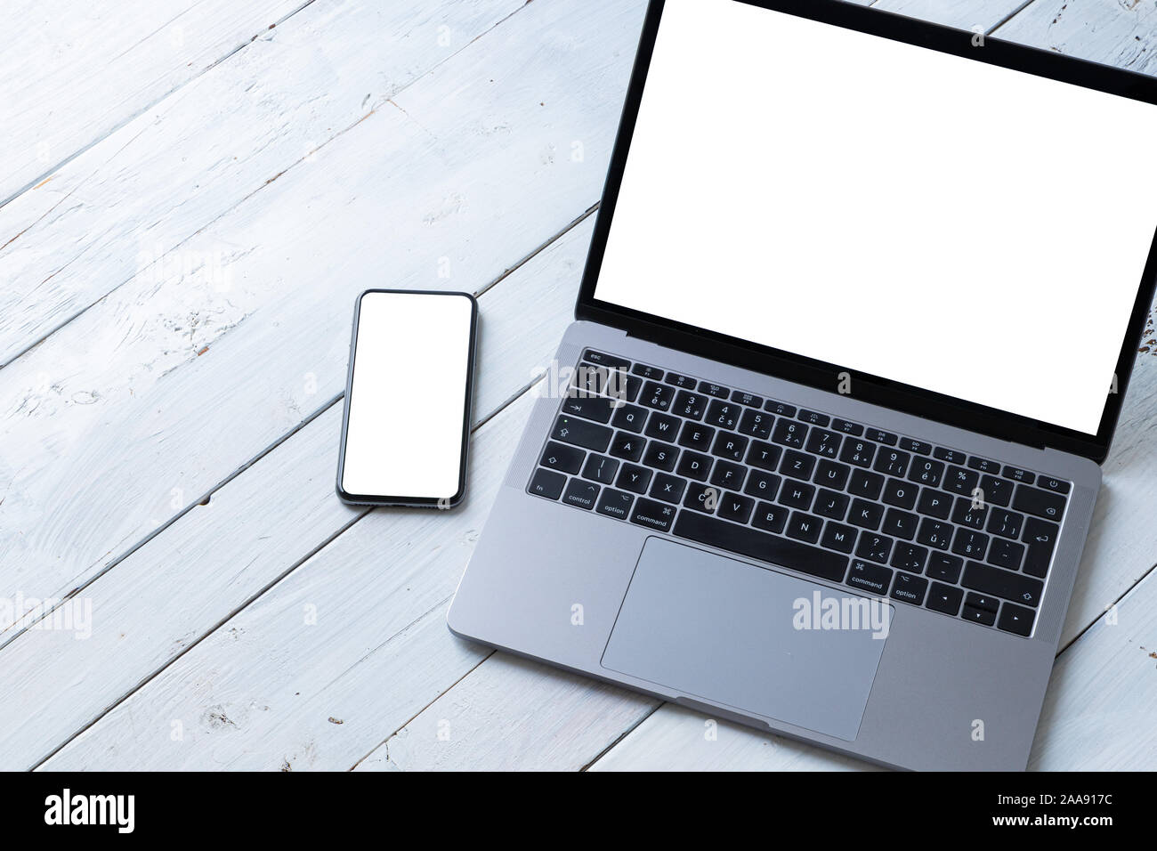 The Laptop and phone with blank screens on white wooden table ...