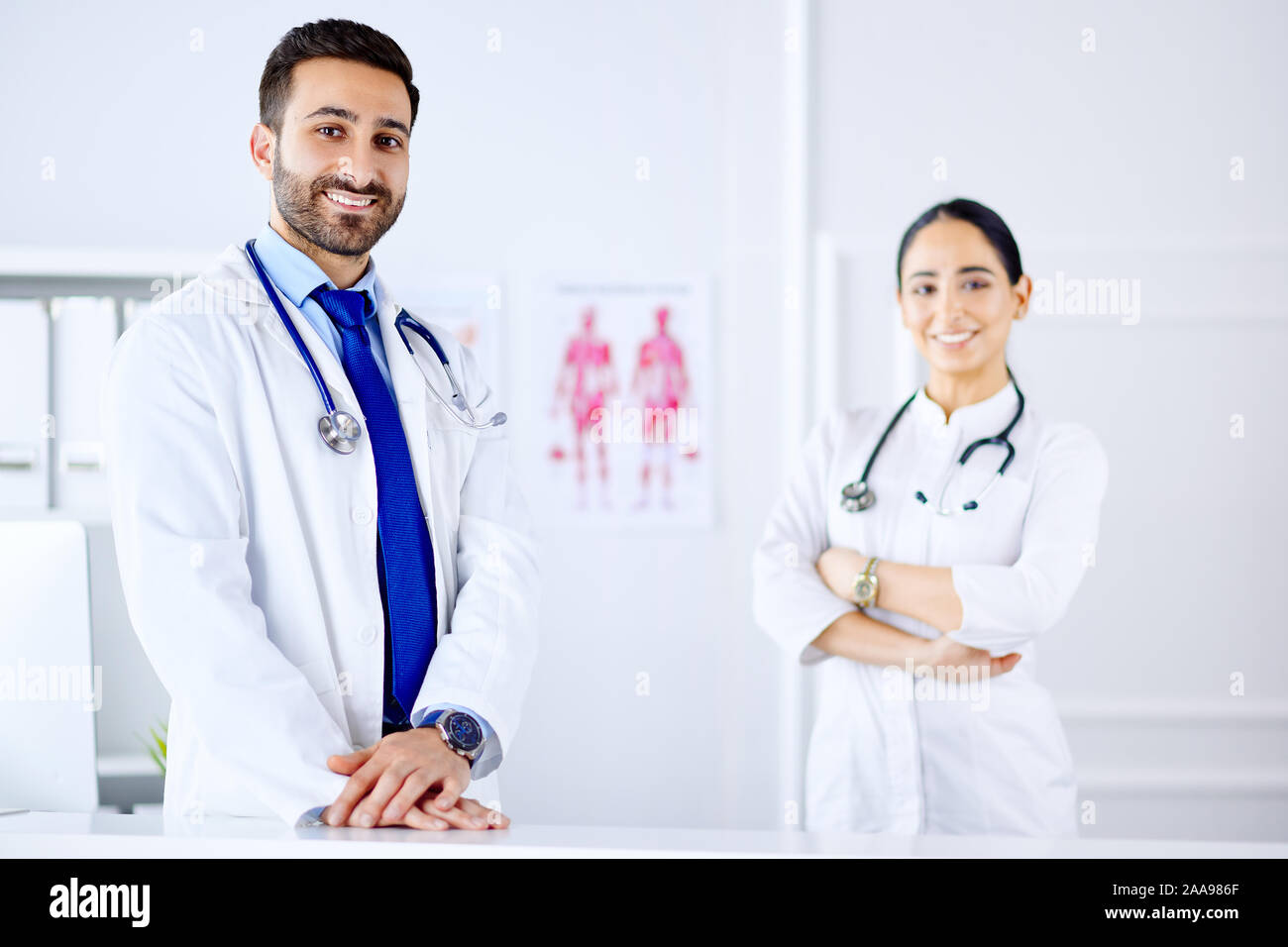 Two young smiling arab doctors standing in consultation room in ...