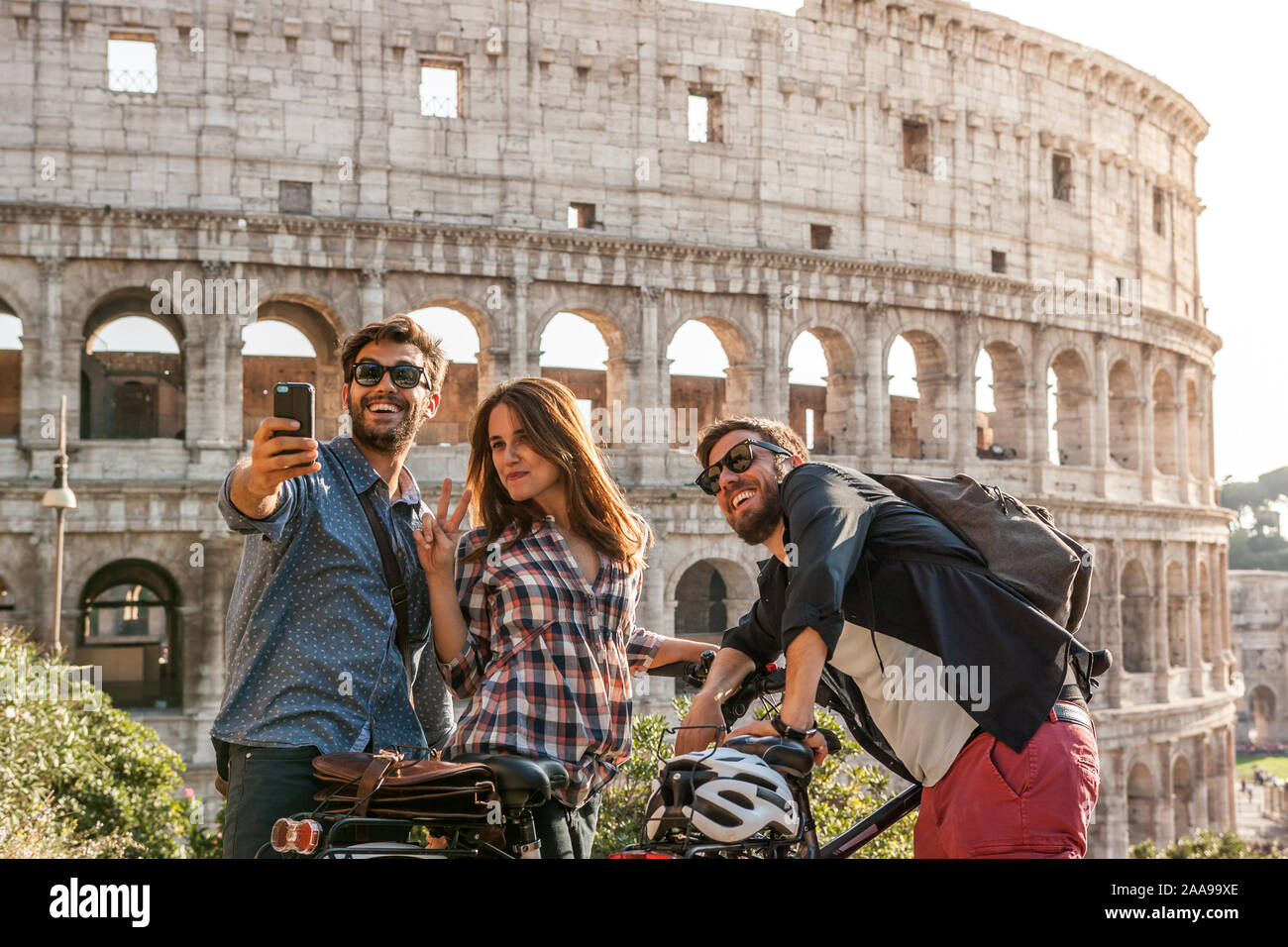 Three happy young friends tourists with bikes at Colosseum in Rome ...