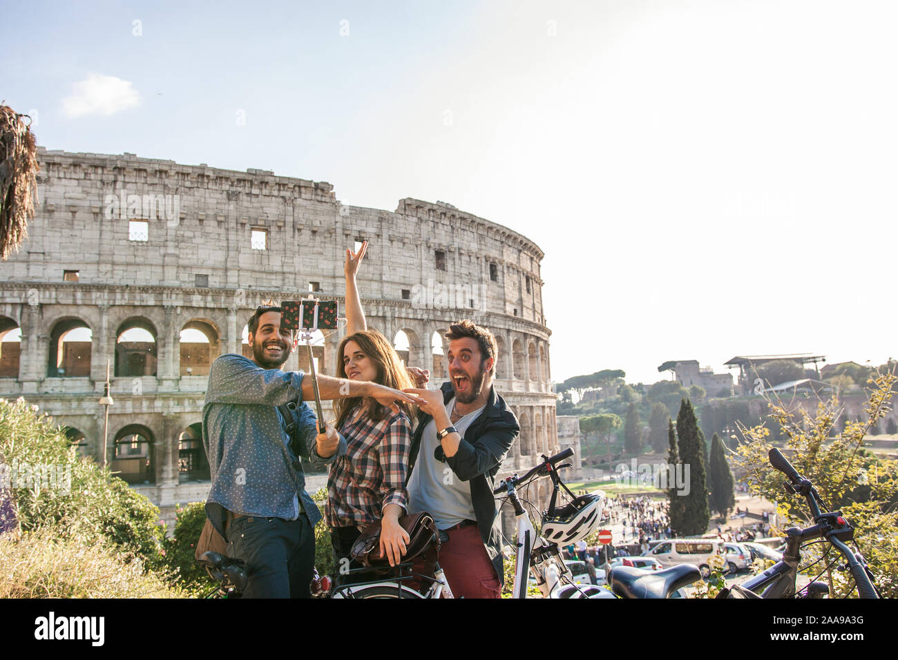 Three happy young friends tourists with bikes at Colosseum in Rome ...