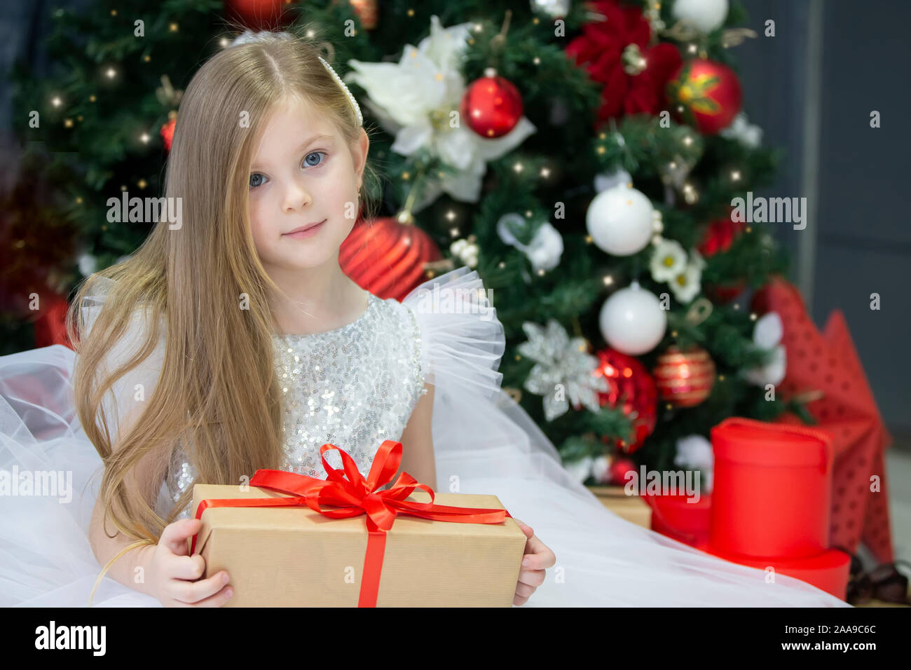 Beautiful child with a christmas gift. Dressing up girl at the New Year ...