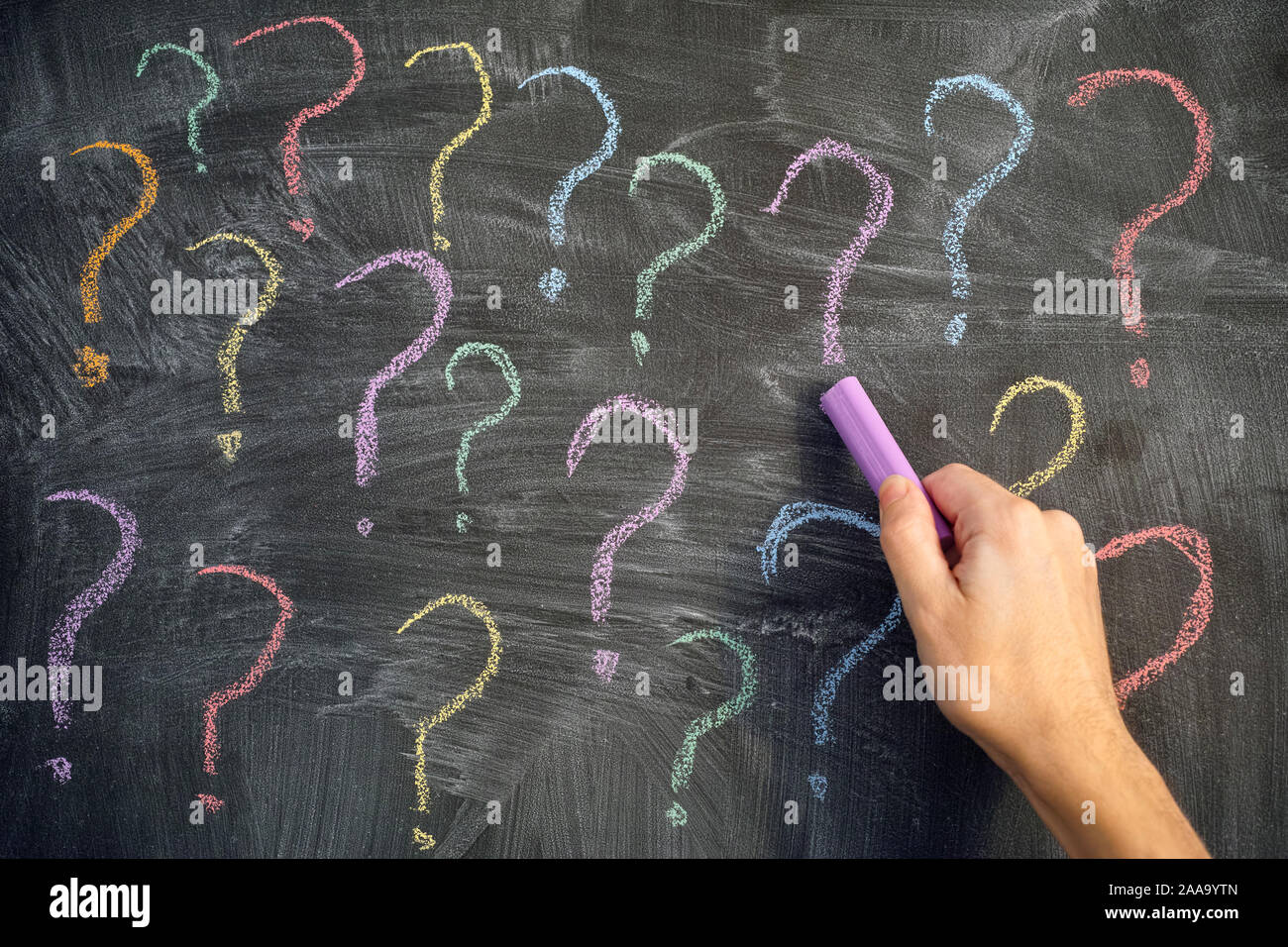 Too many questions. Man drawing colorful question marks on a blackboard ...