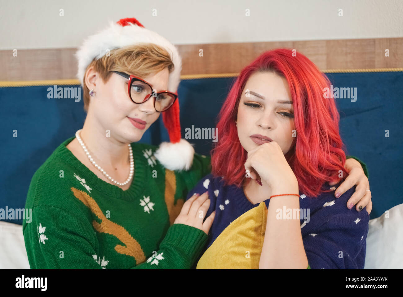 two sad unhappy girls sitting on the bed and hugs on christmas holiday ...