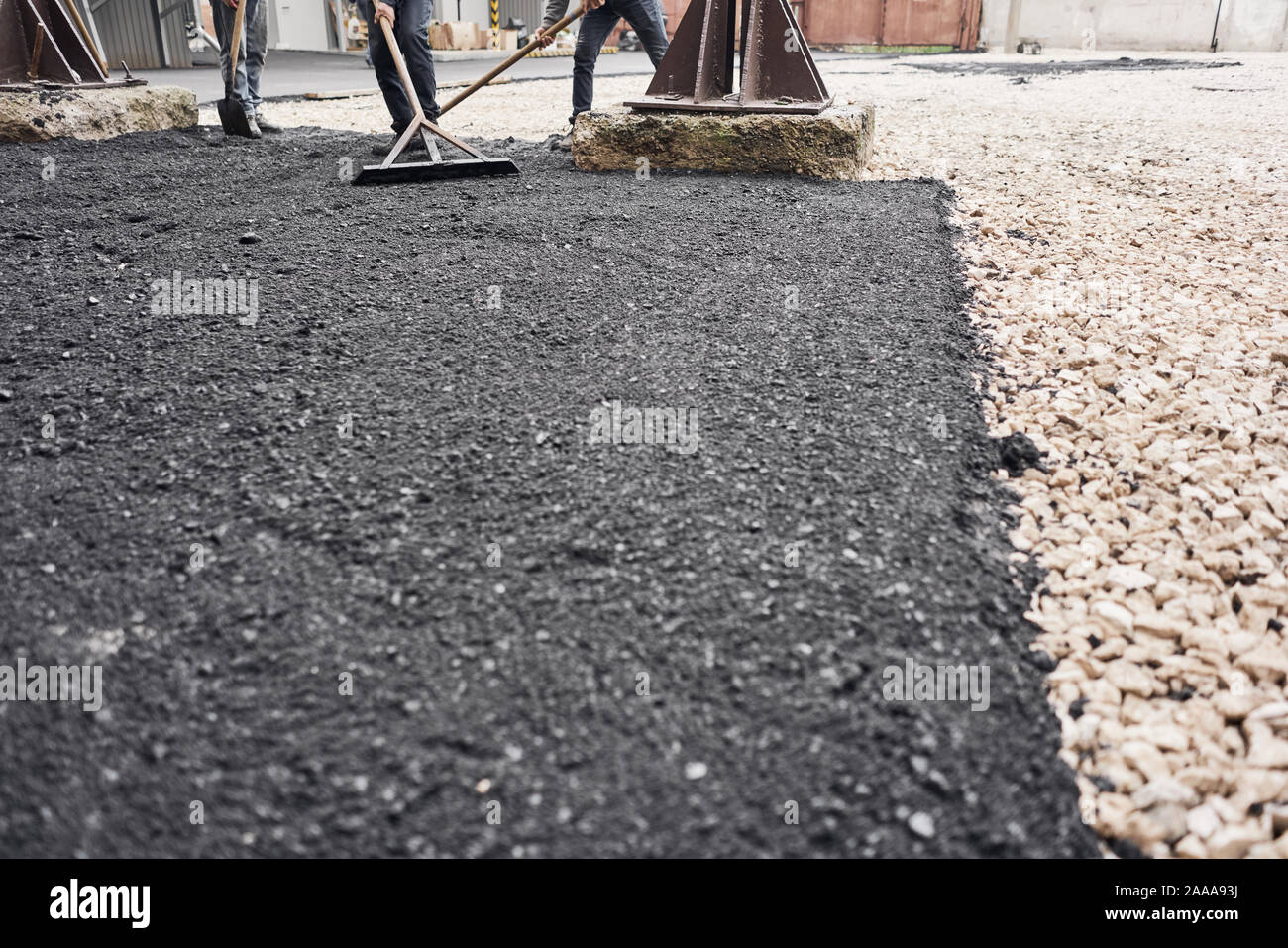 Laying new asphalt, covering the pit, on the rubble. Workers carry in ...
