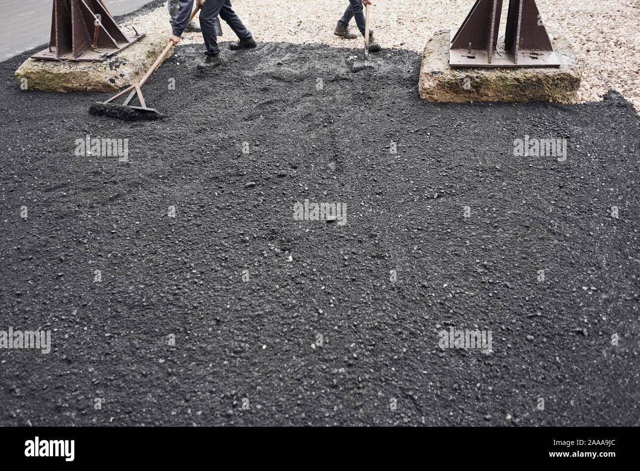 Laying new asphalt, covering the pit, on the rubble. Workers carry in ...