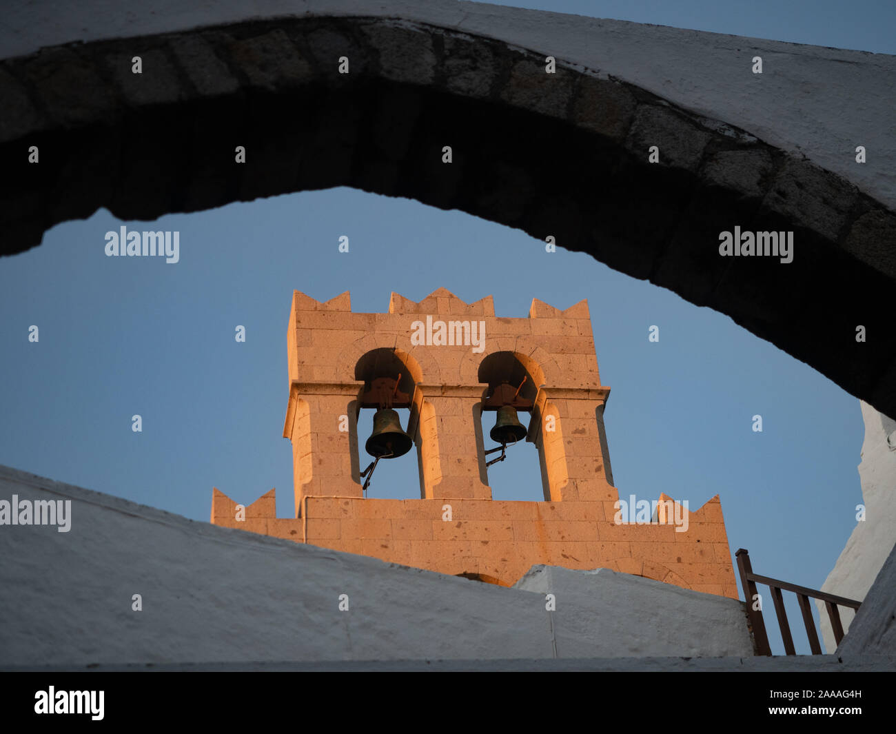 A sunlit bell tower and two bells seen beneath a masonry arch in the ...