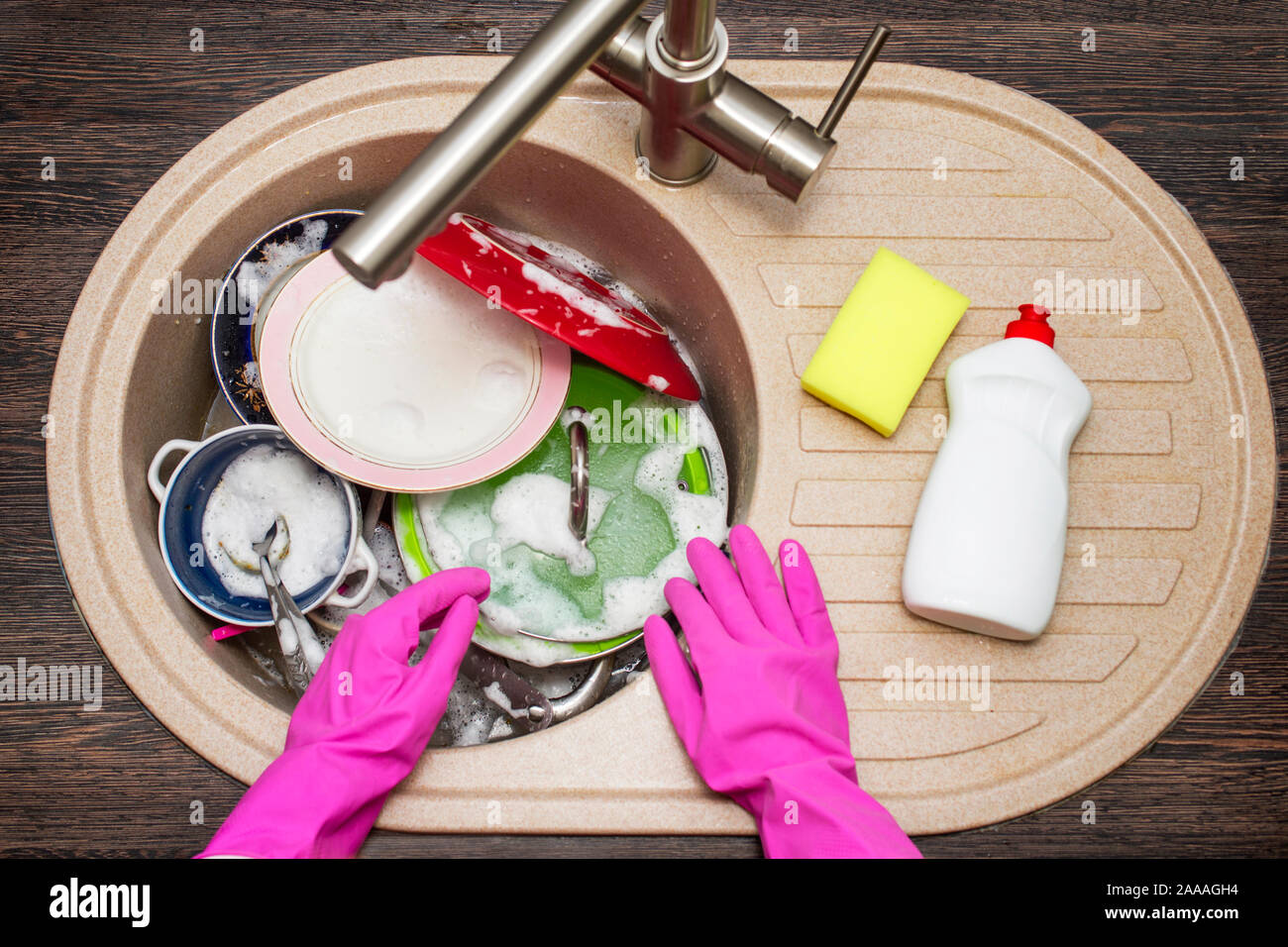 Close up hands of woman washing dishes in kitchen. Hands in red rubber ...